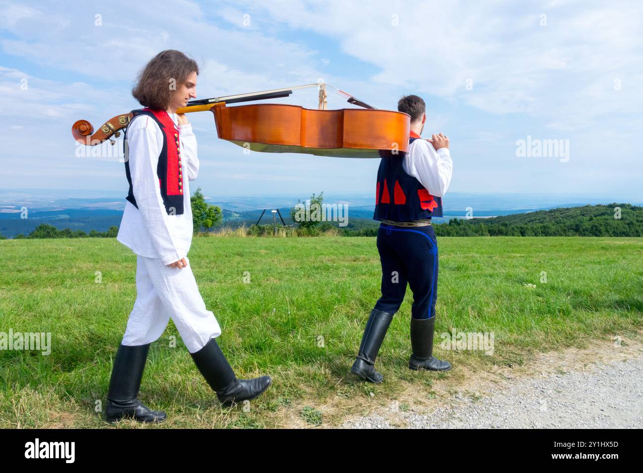 Two men in folk costumes carrying Musical Instrument Contrabass Strání ...