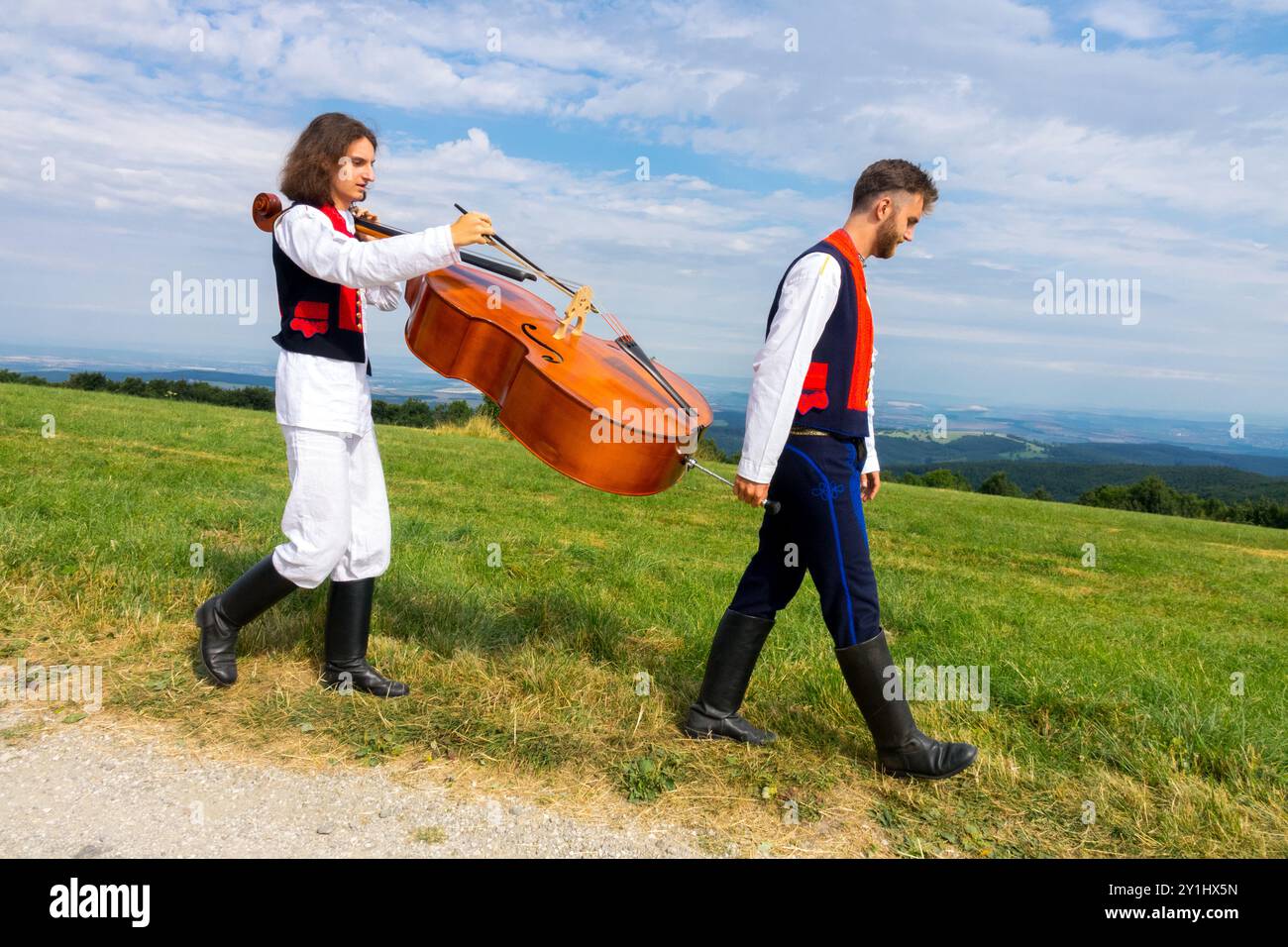 Two men in folk costumes carrying Musical Instrument Contrabass and ...