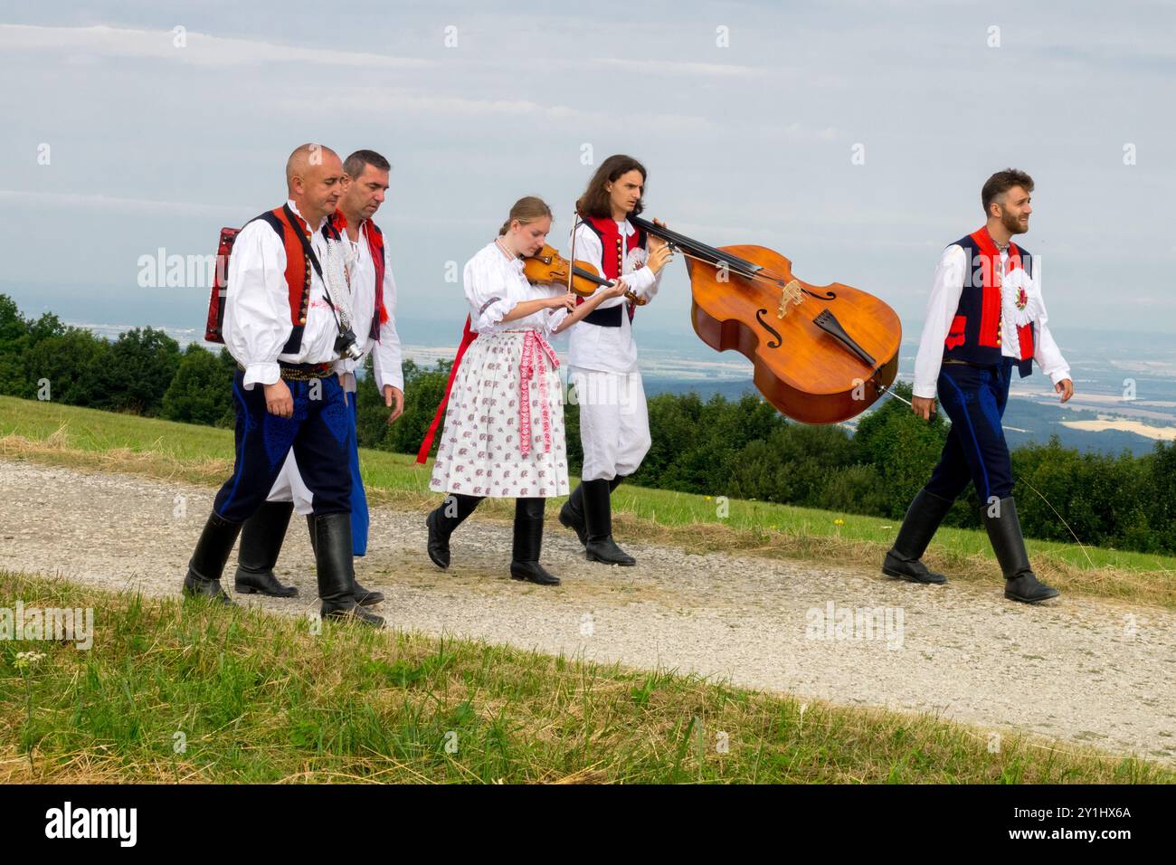Group of musicians in traditional folk costumes walking along a rural ...