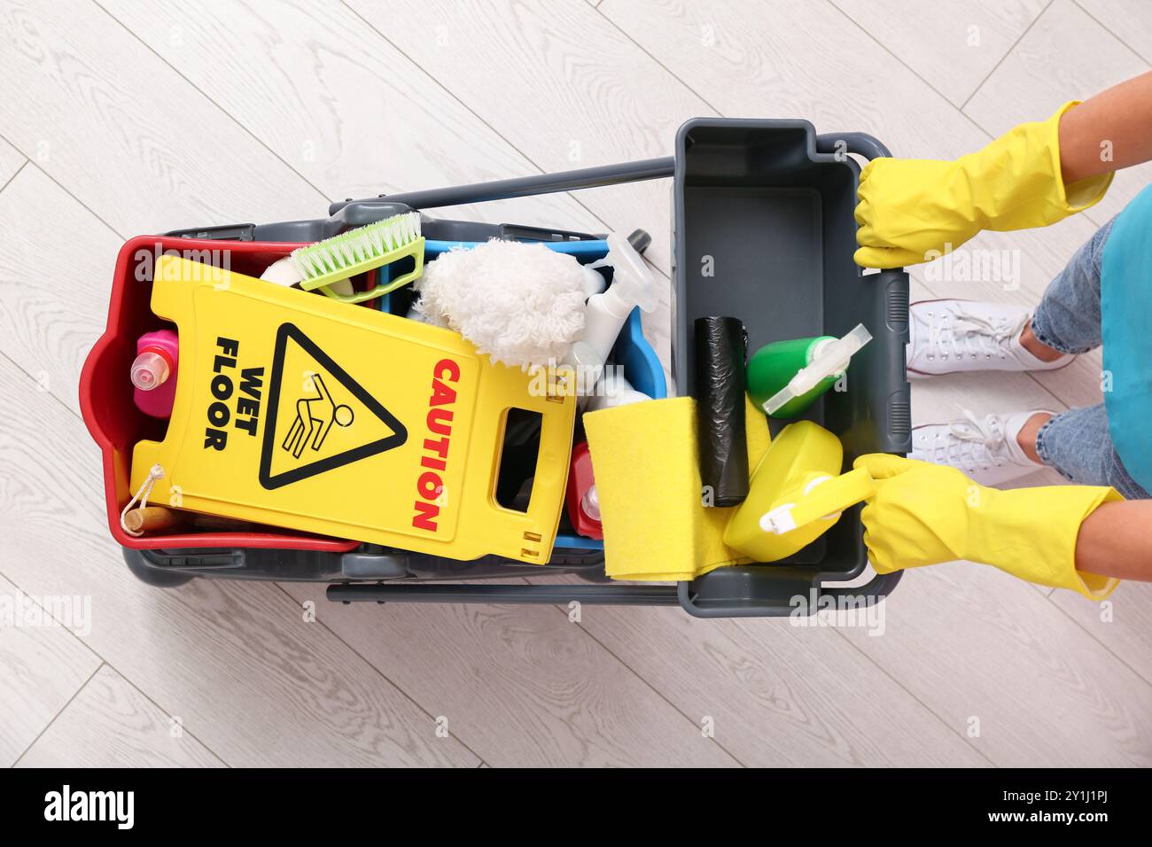 Janitor pushing trolley with cleaning supplies and caution sign, top ...