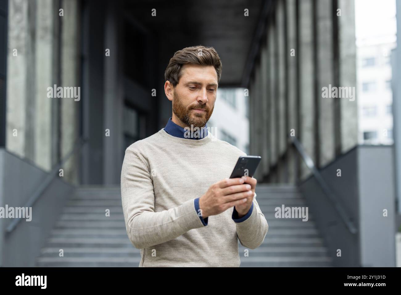 Serious man using phone outside modern office building. Reflects focus ...