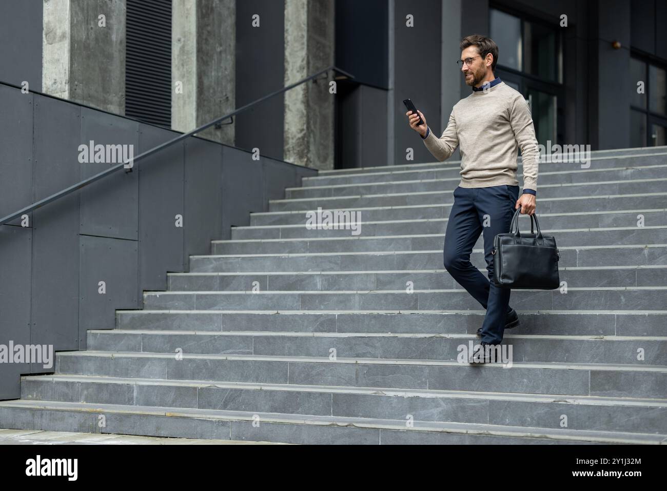 Businessman walking down grey concrete steps using smartphone, dressed ...