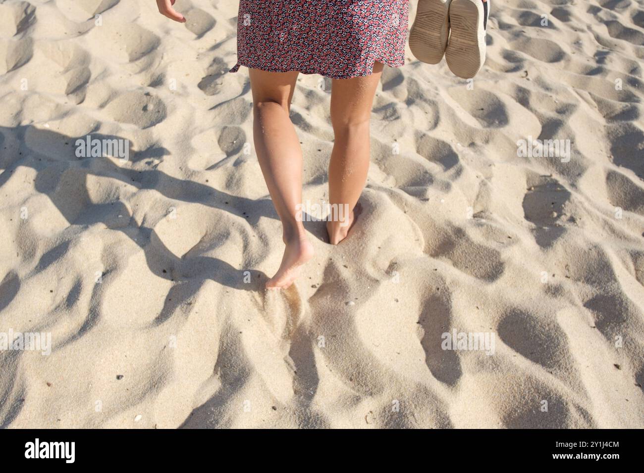 Woman In A Sundress Seen Hip Down From Behind As She Walks Barefoot On