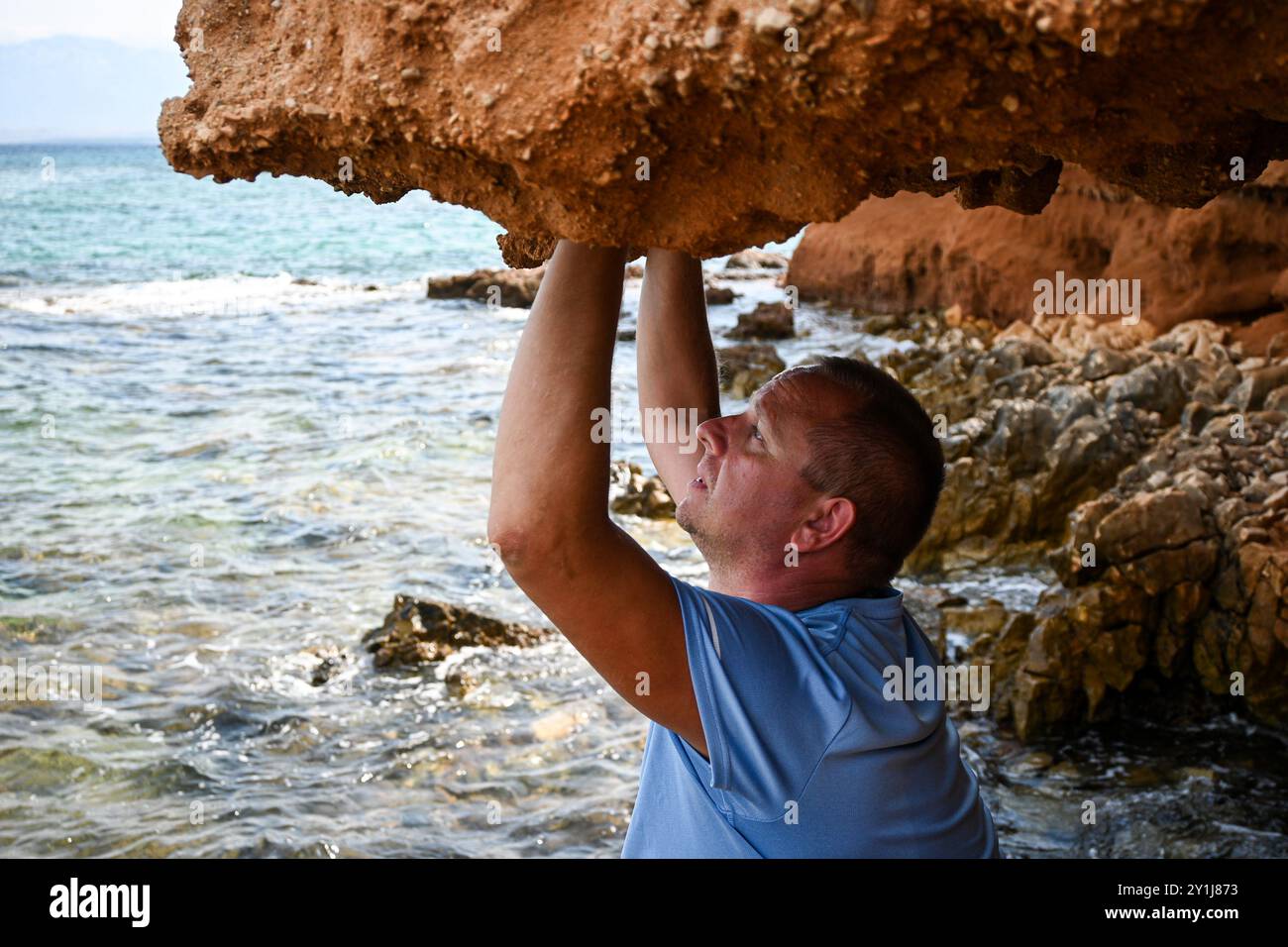 Tourist is exploring a cave by the sea, holding a rock and observing ...