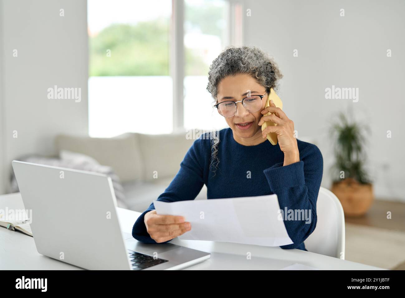 Busy middle aged woman working from home making phone call checking ...