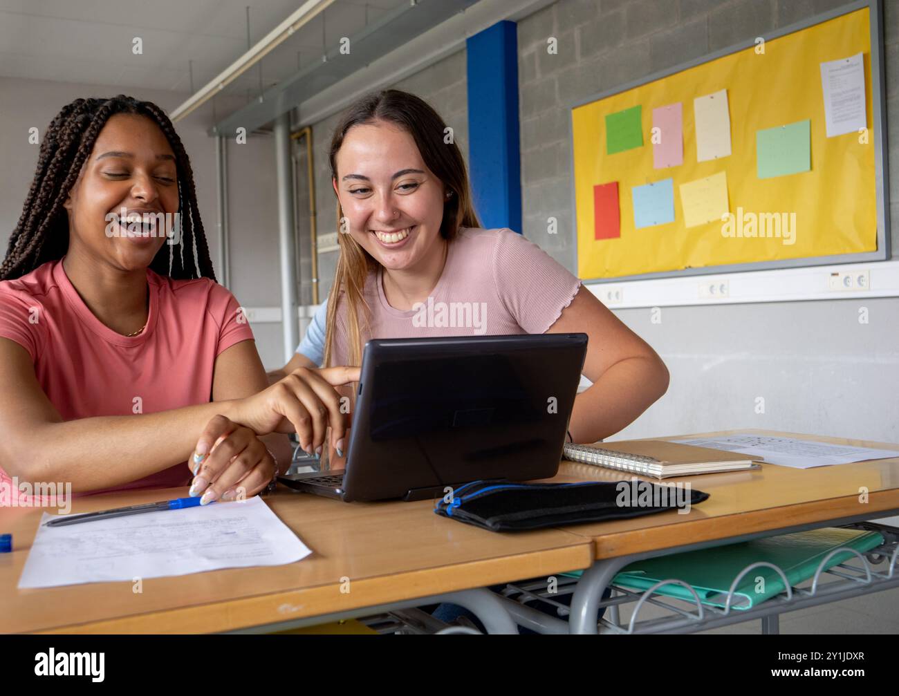 Two multiethnic teenage girls in class doing a joint project with a ...