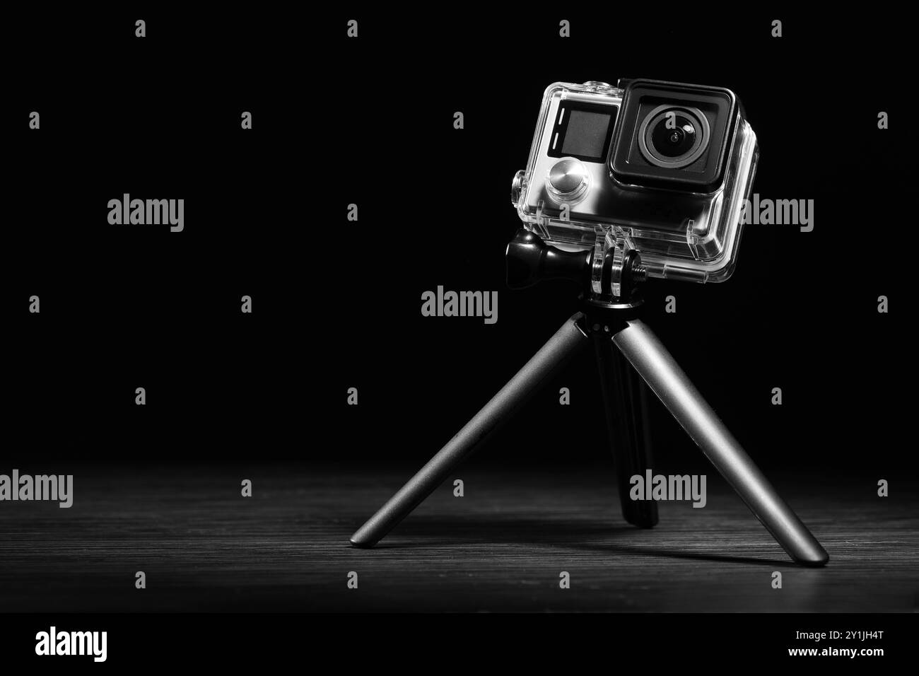 Modern action camera and tripod on wooden surface against black ...