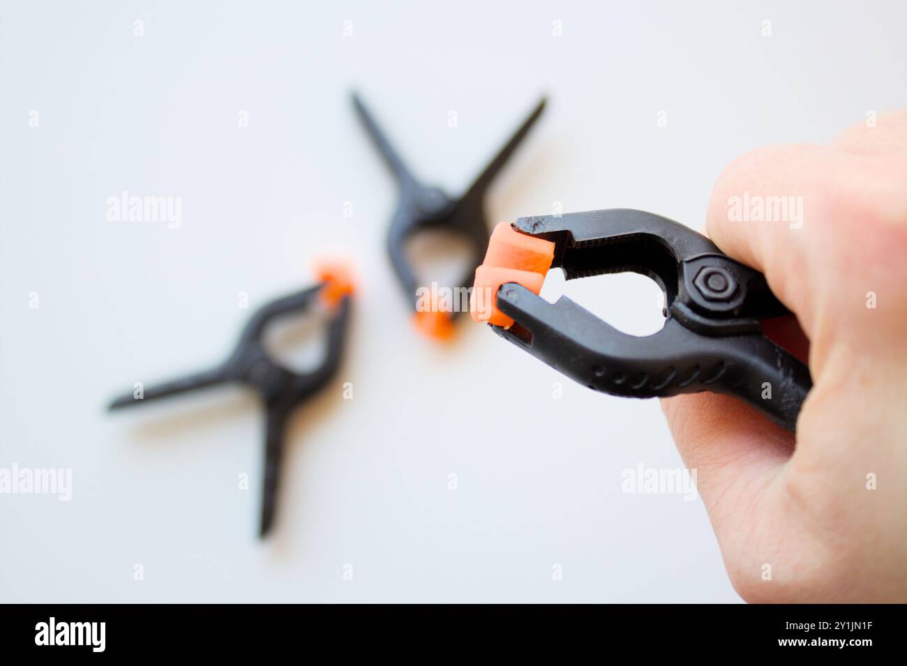 Caucasian hand holding a plastic spring clamp over white background ...
