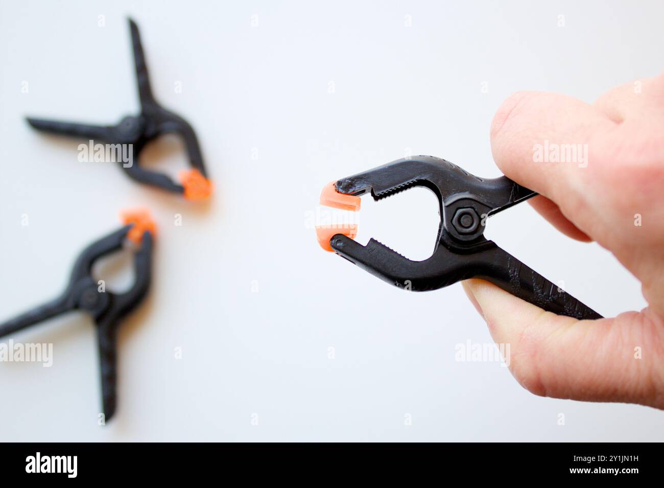 Caucasian hand holding a plastic spring clamp over white background ...