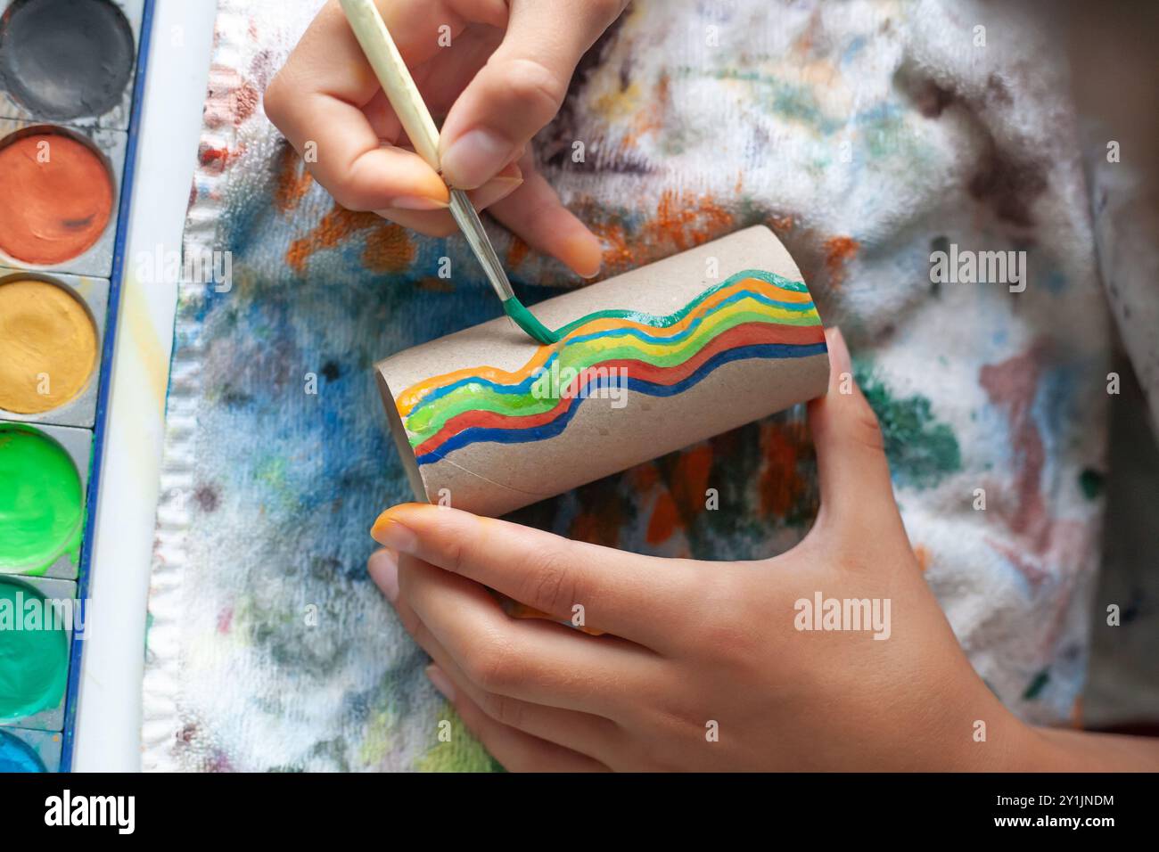 Child painting on toilet paper roll with a green brush to make a rocket ...