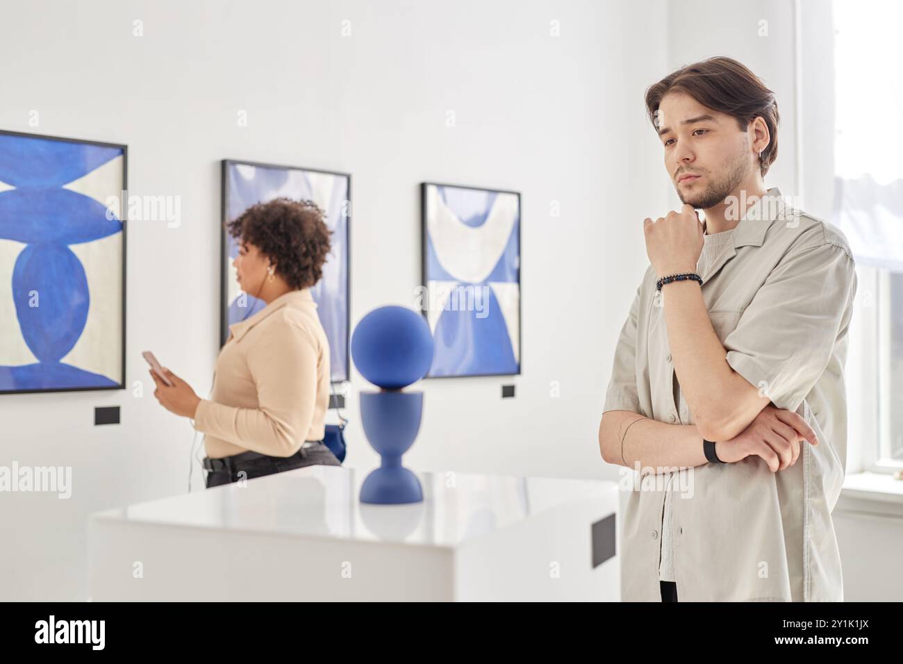 Minimal portrait of young man looking at modern art sculpture while ...
