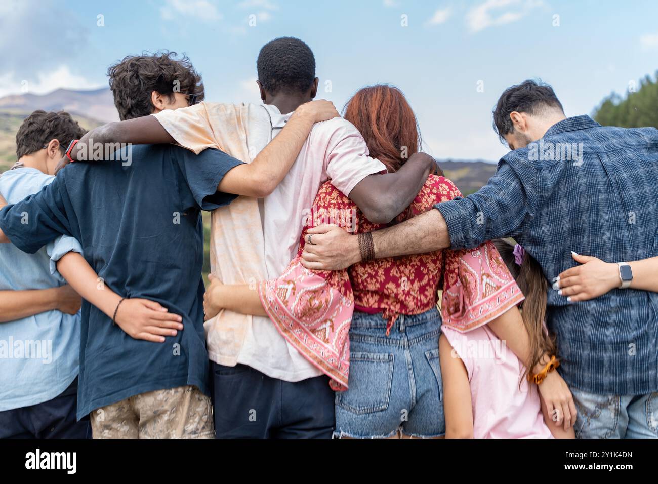 Rear view of diverse group of friends embracing while enjoying nature ...