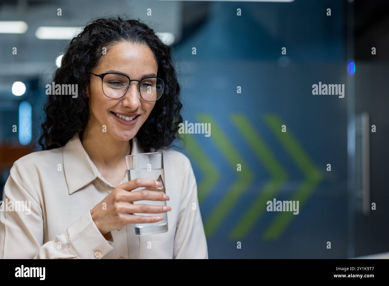 Hispanic businesswoman sitting at office desk holding glass of water ...