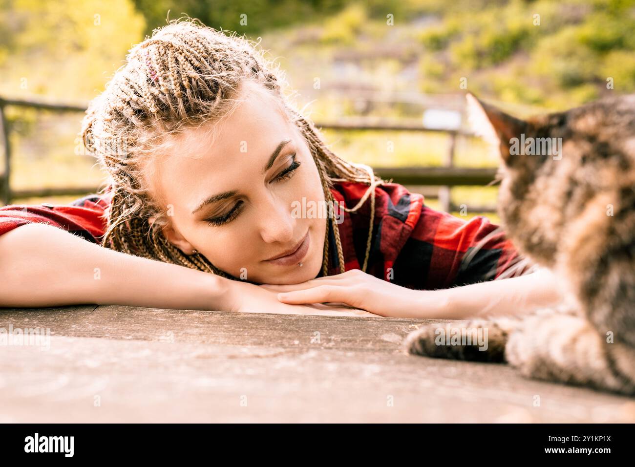 Young woman with braids is resting her head on her arms on a wooden ...