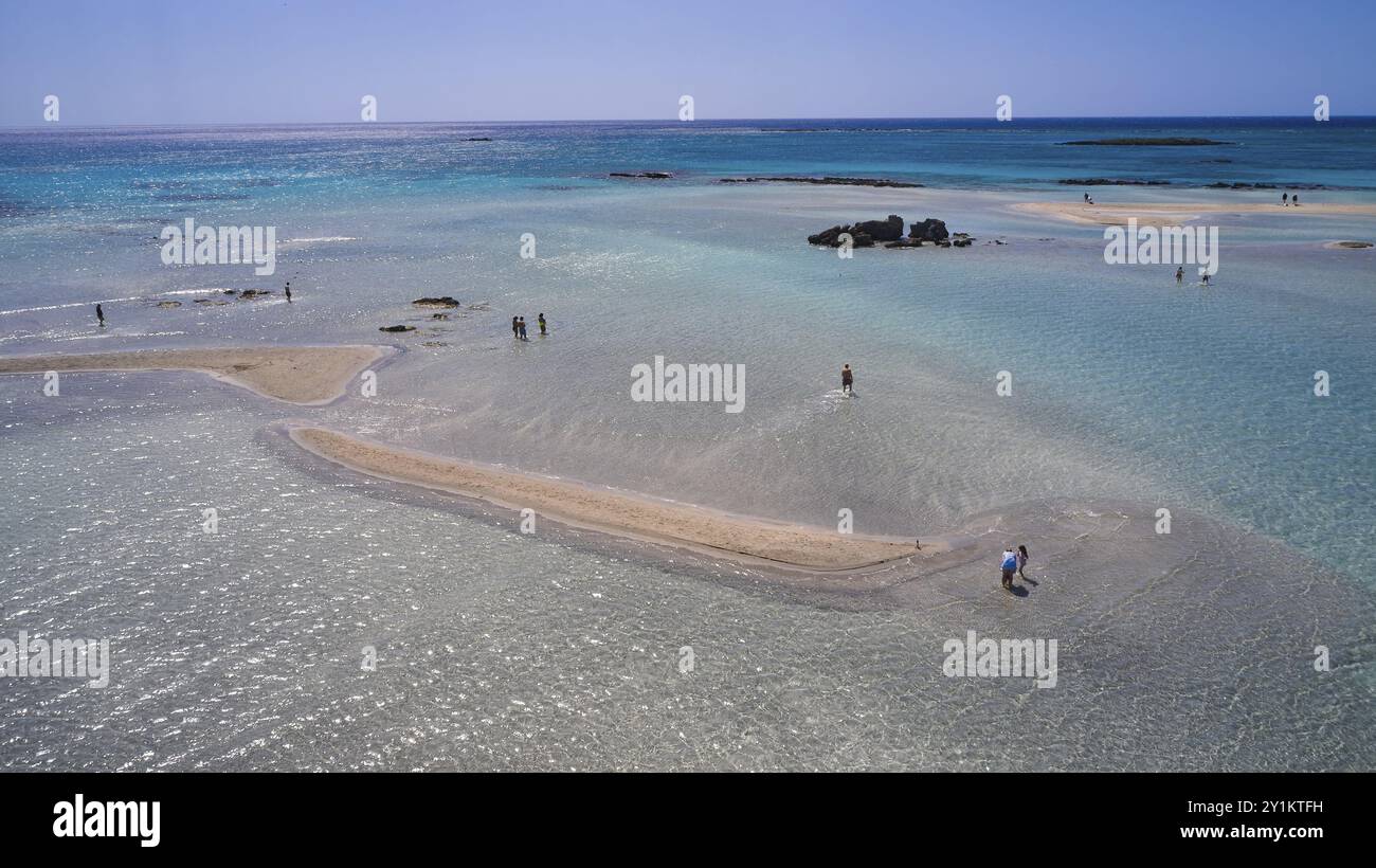 Sandbank in clear, calm sea with scattered people enjoying the natural surroundings, Elafonissi ...