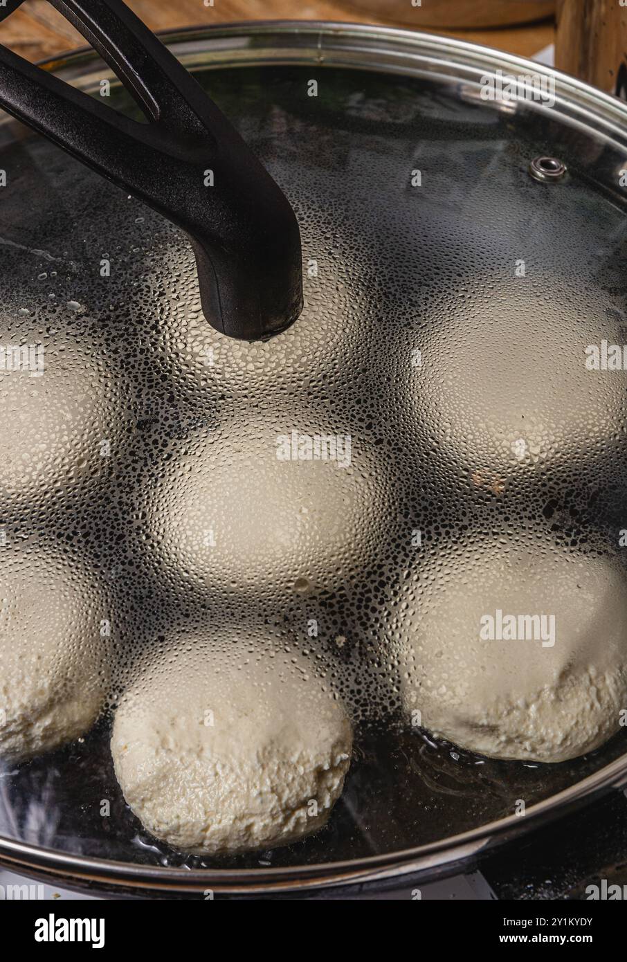 Cottage cheese pancakes are fried in a frying pan with a lid Stock ...