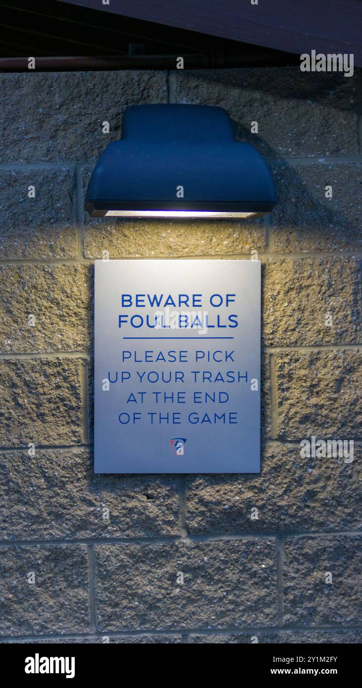 Beware of foul ball sign on a brick wall at a baseball field lit by a ...