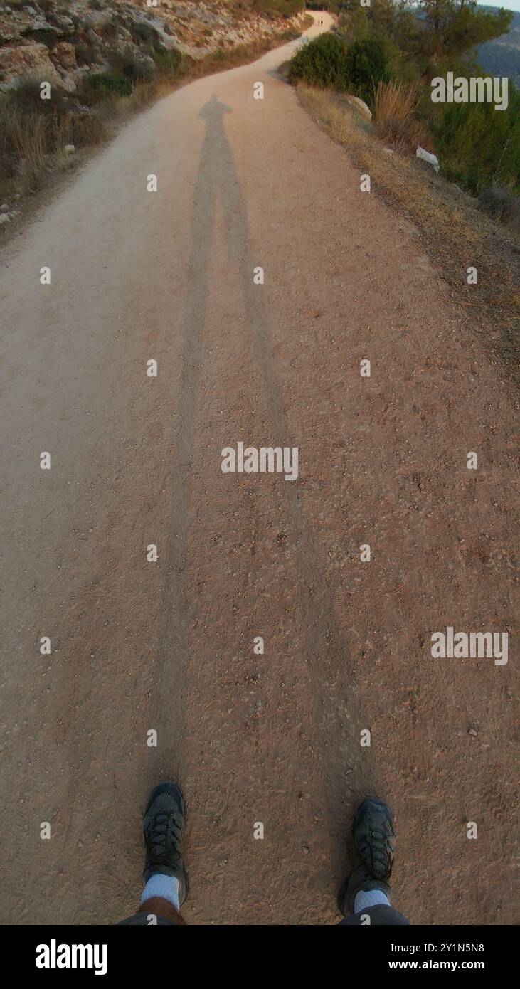 Lengthy shadow of a man's legs on an orange, dirt pathway through a ...