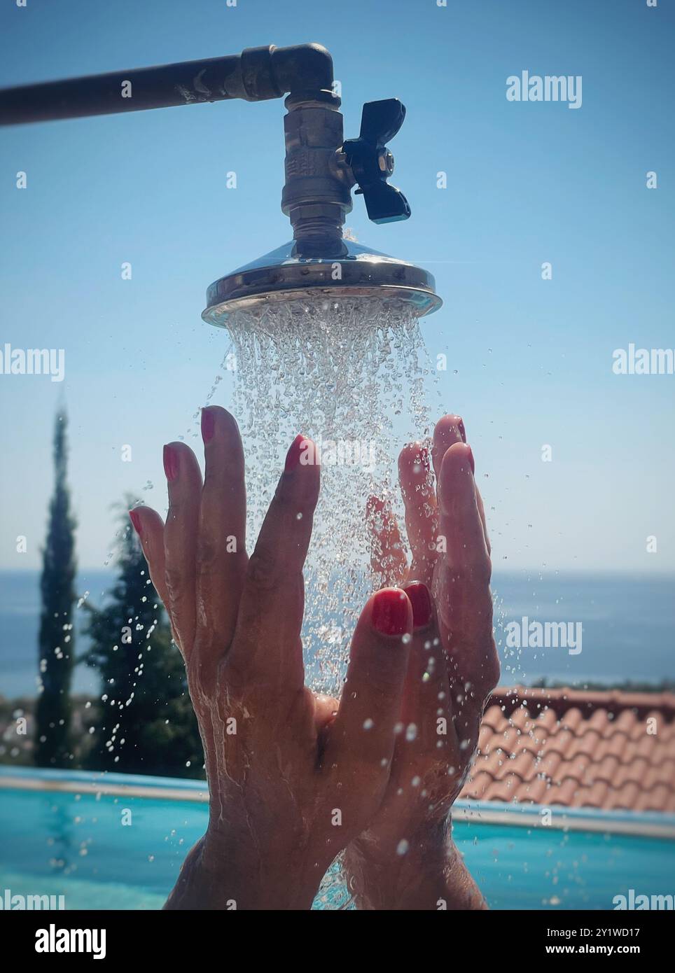woman testing the water of an outdoor shower at a pool on the island ...