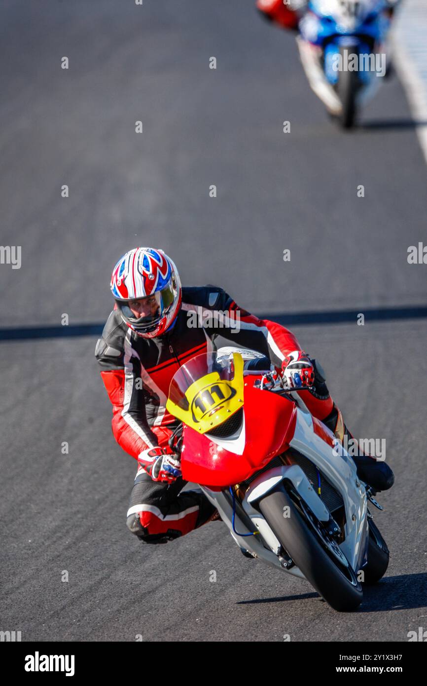 A motorcyclist in racing gear speeds around a curve on a racetrack ...