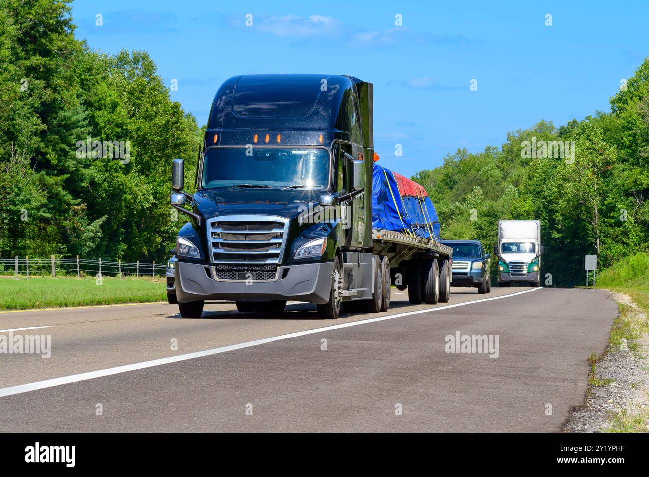 Horizontal shot of a black flatbed eighteen wheeler semi carrying a ...