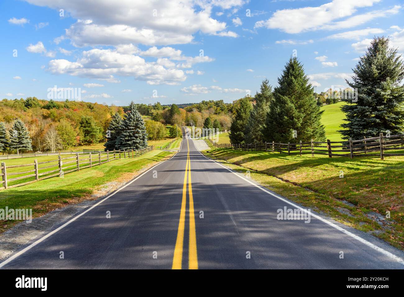 Empty road between fenced fields in a rolling rural landscape on a ...