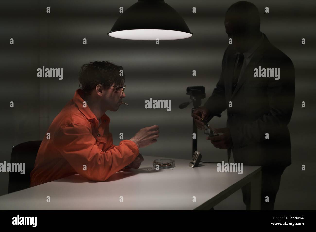 Officer in black suit interrogating seated suspect in orange jumpsuit ...