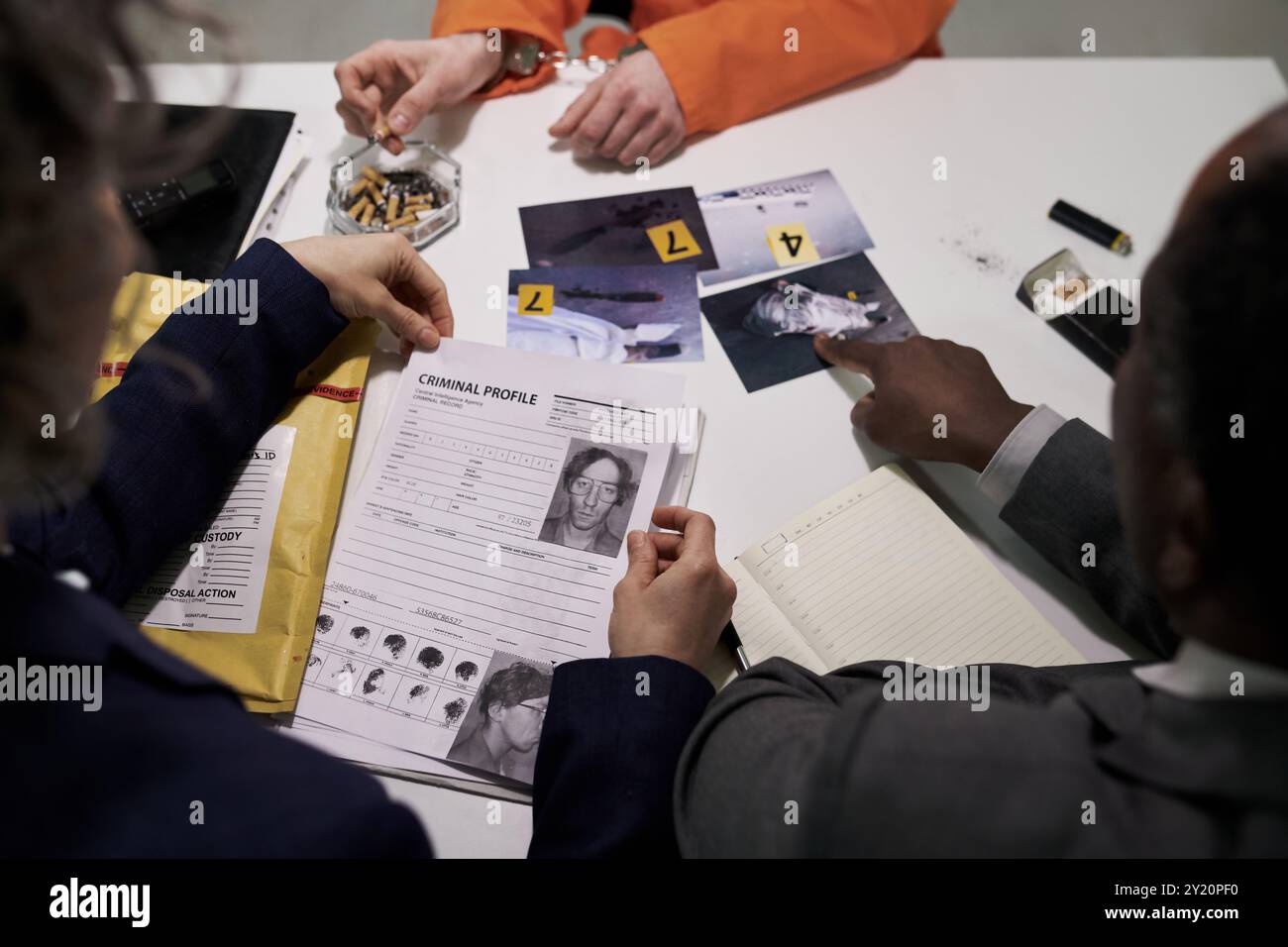 Investigators examining criminal profiles and evidence at desk filled ...