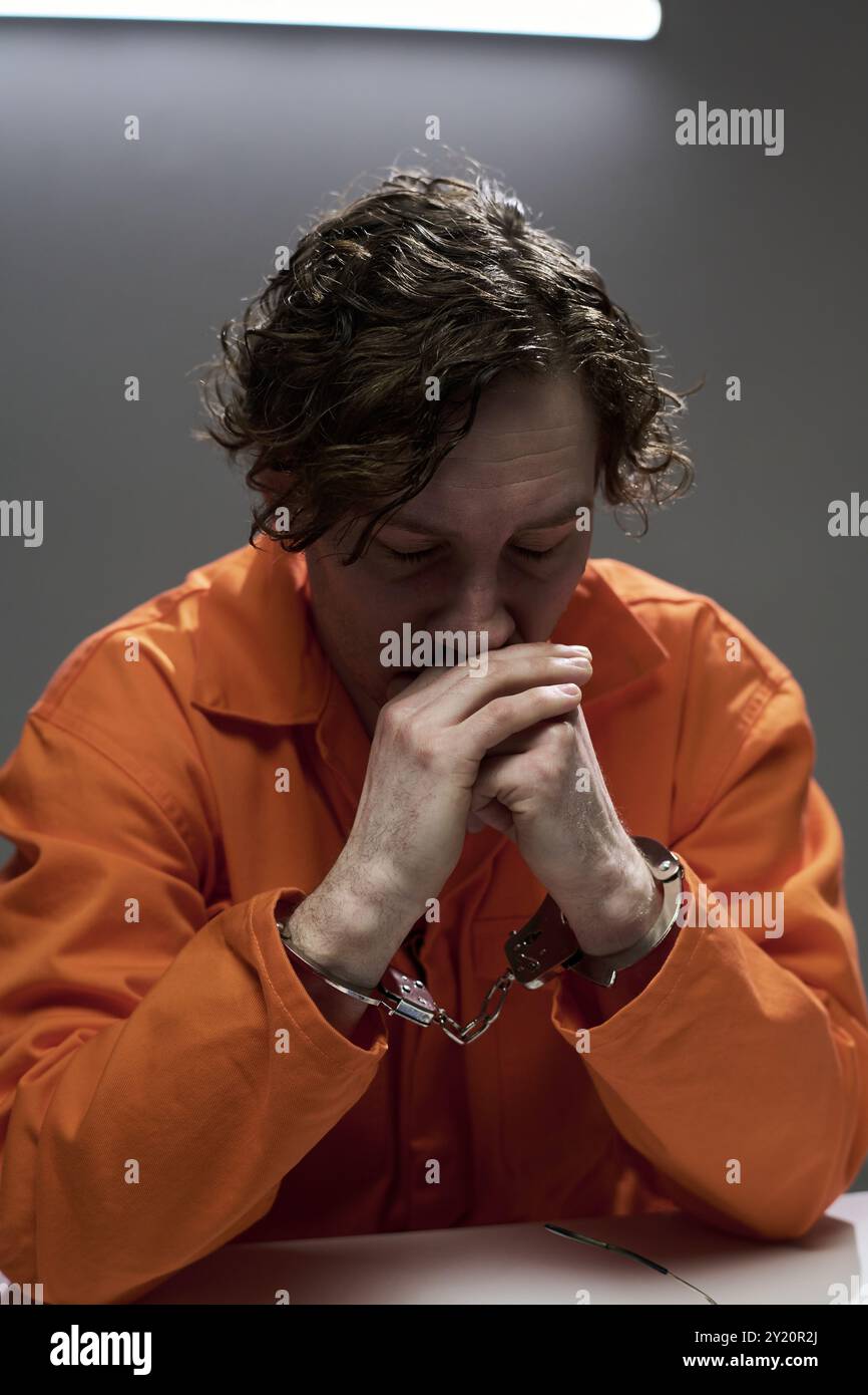 Pensive man wearing orange jumpsuit and handcuffs sitting alone at ...