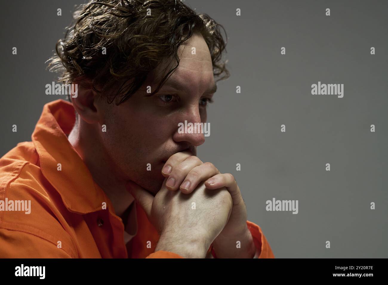 Contemplative man wearing orange jumpsuit resting chin on hands ...