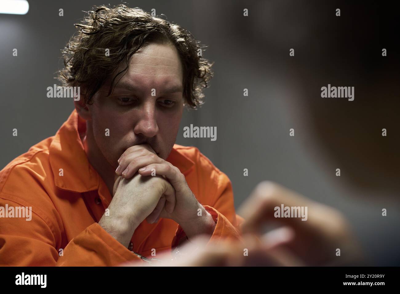 Person wearing orange prison uniform sitting with hands clasped under ...