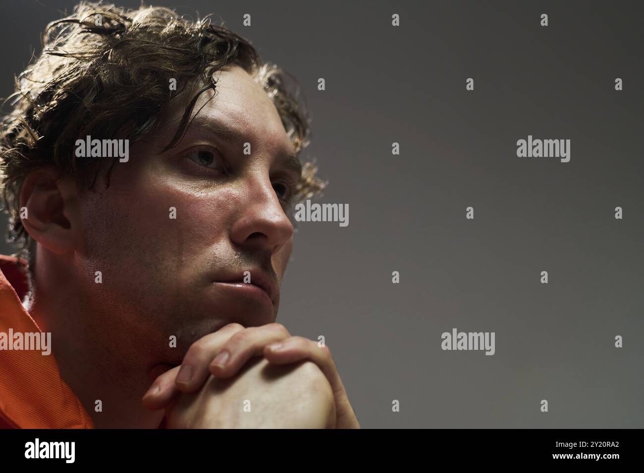 Portrait of young Caucasian man resting his chin on clasped hands while ...