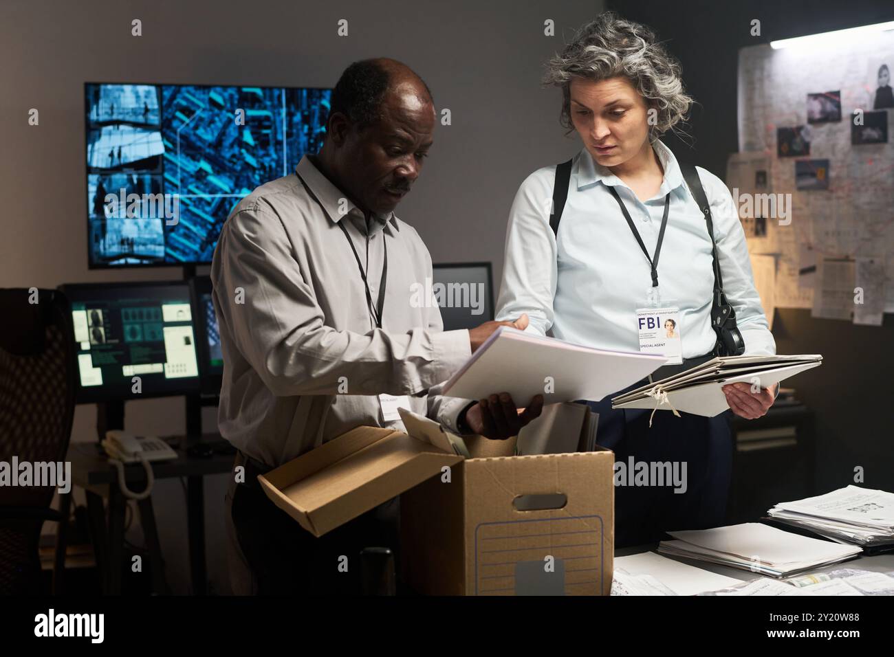 Investigators standing in an office wearing badges reviewing case ...