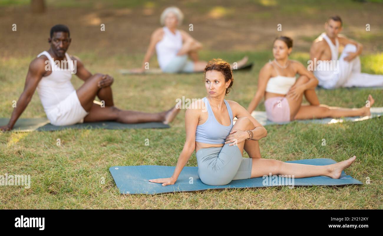 Multinational yoga enthusiasts with female coach perform wakrasana in ...