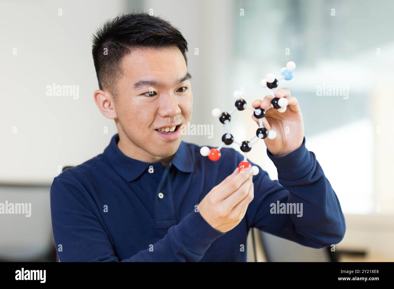 A young student is holding up a molecule model and observing it happily in the classroom for ...