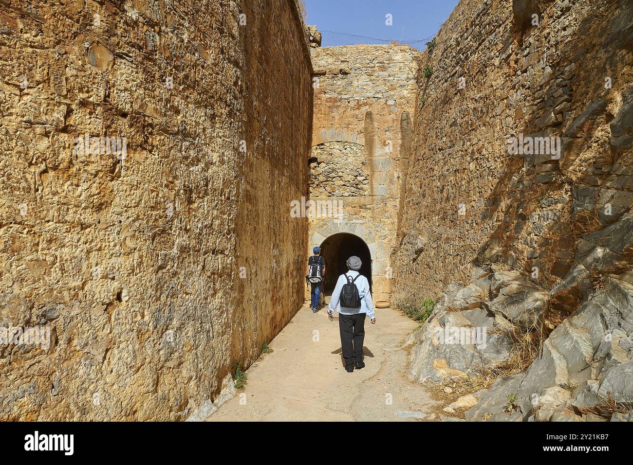 Two people walking through a narrow passageway between high stone walls ...