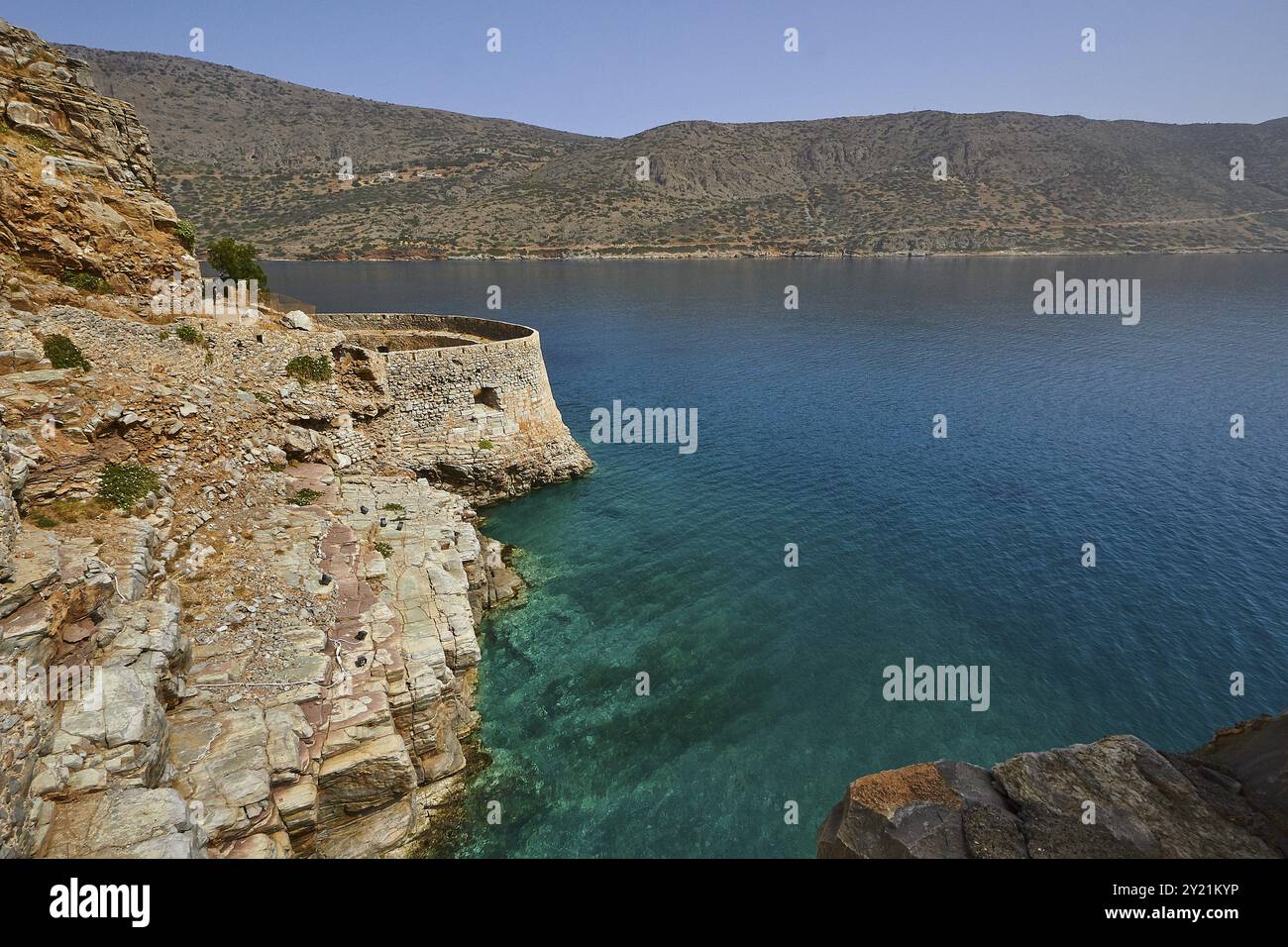 Rustic stone wall on cliffs above a turquoise sea with mountains in the ...