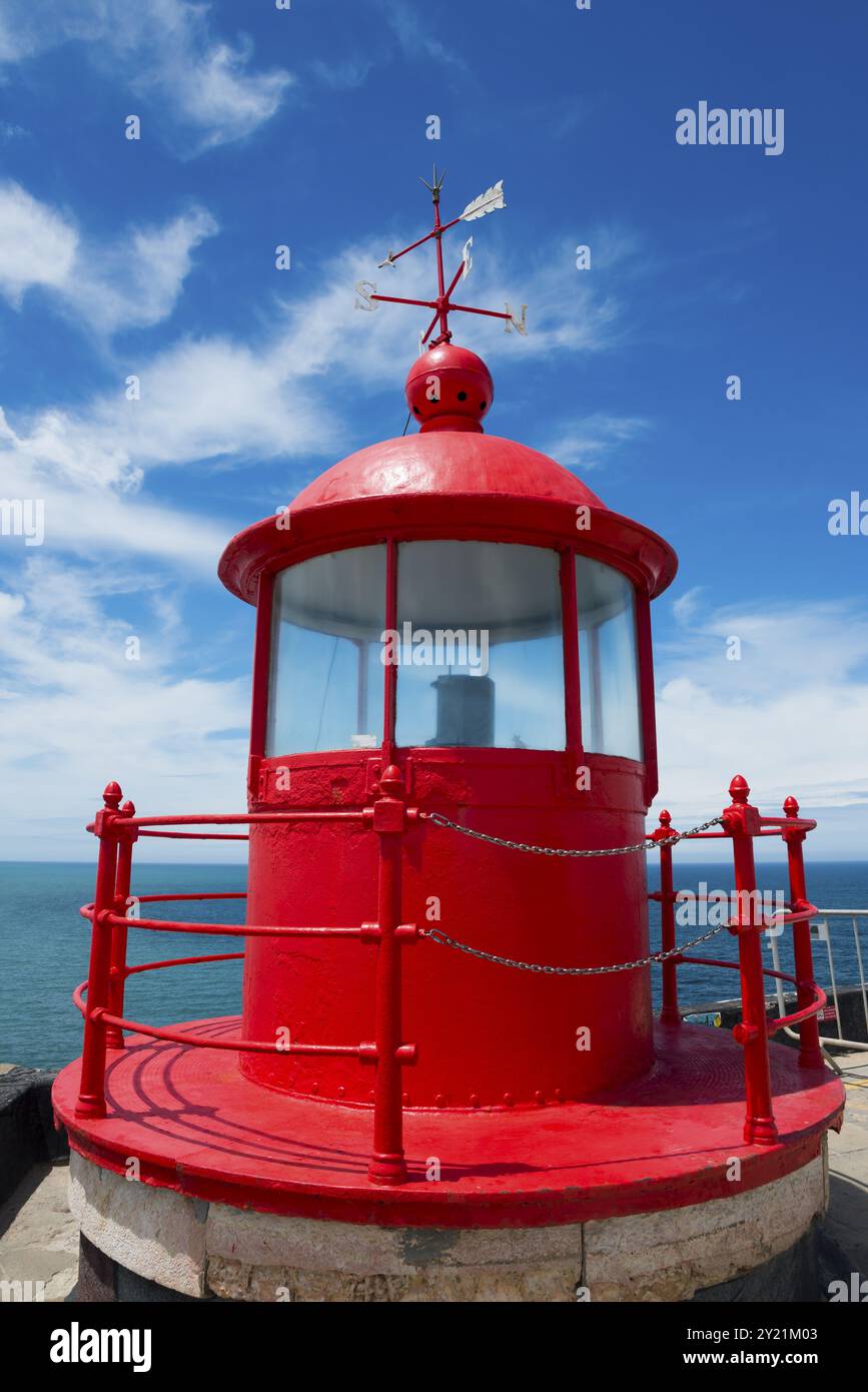 Red lighthouse with round roof on a coastal platform, blue sky and sea ...
