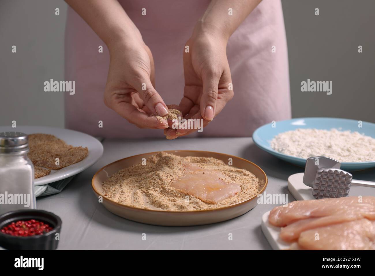 Making schnitzel. Woman coating slice of meat with bread crumbs at grey ...