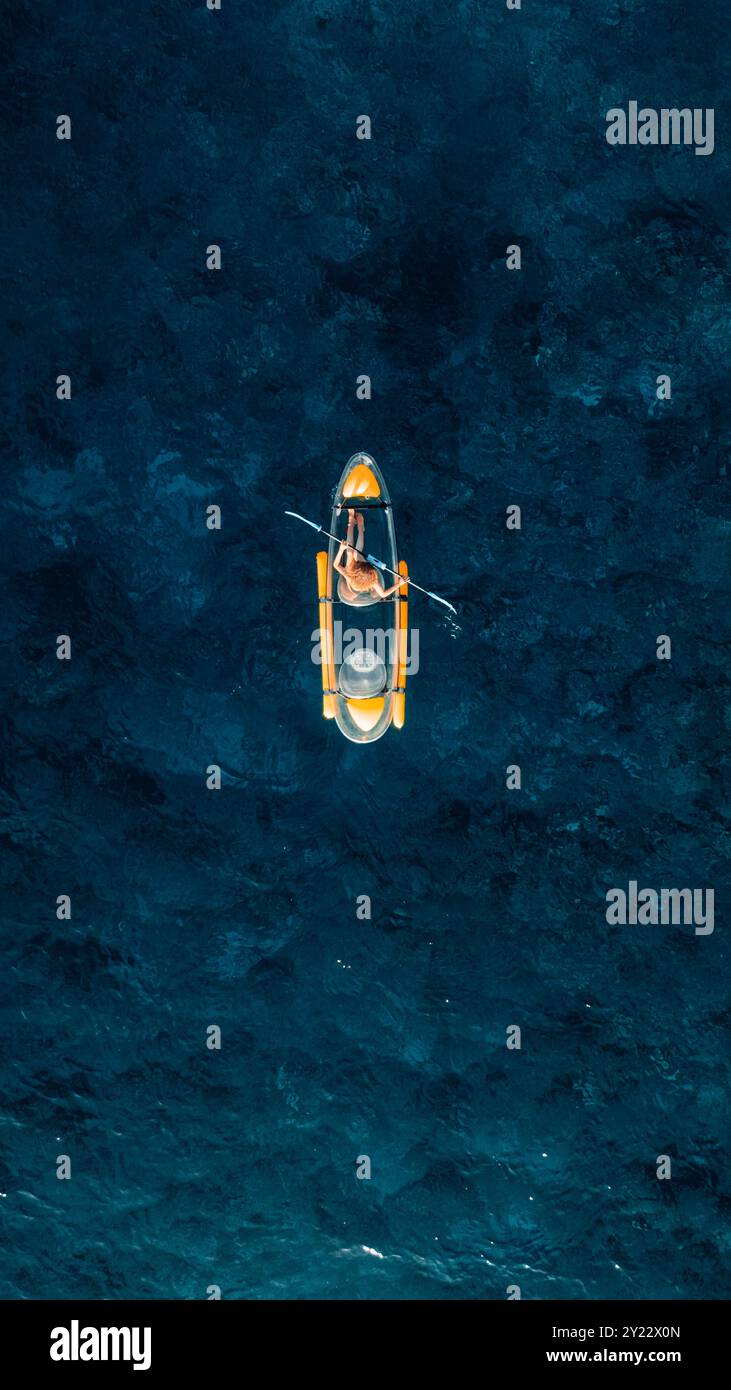 Vertical shot: Woman on transparent kayak in tropical blue ocean. Drone ...