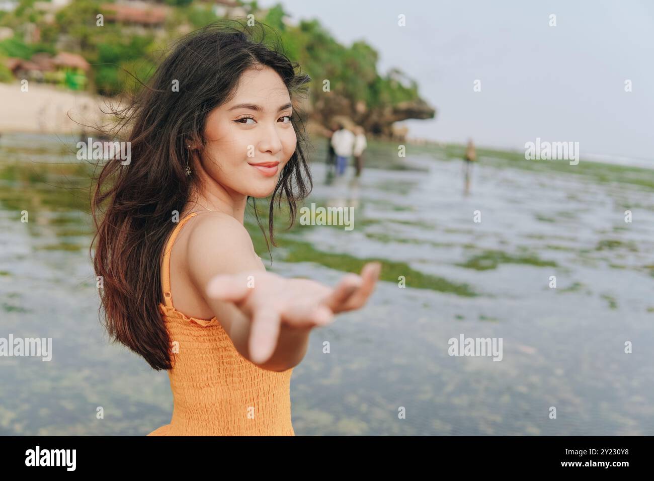 Smiling young Asian woman wearing an orange dress doing invite hand ...