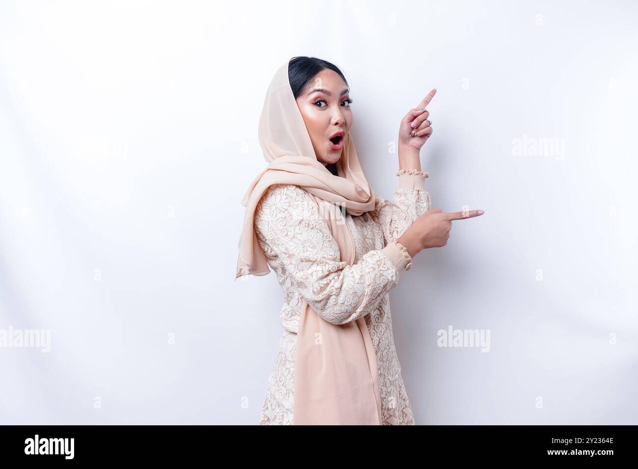 Shocked Asian Muslim woman pointing at the copy space on beside her ...