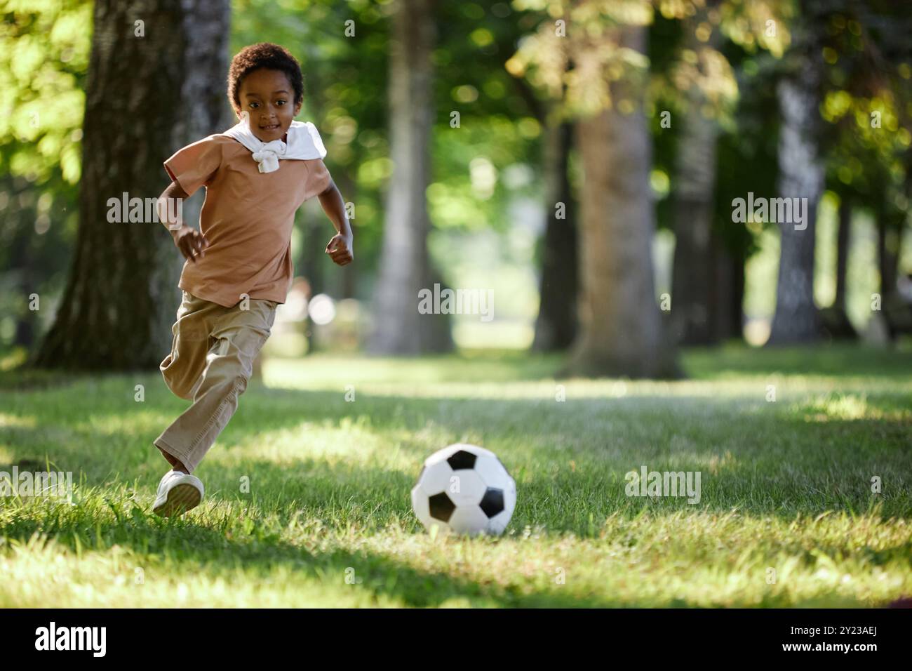 African American boy running on grass in park, he playing football ...