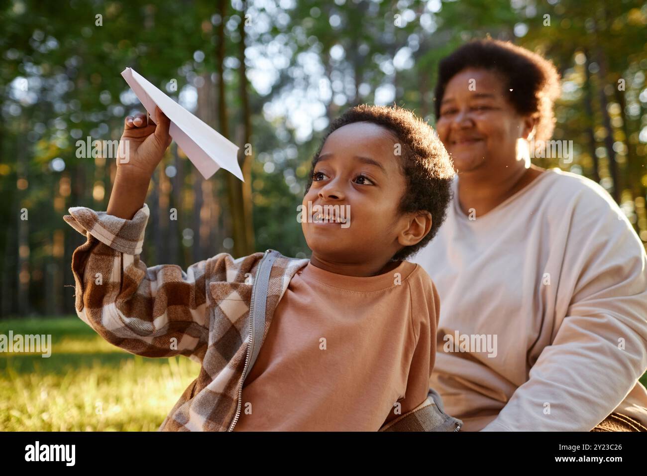 Medium close up of African American boy flying paper airplane while his ...
