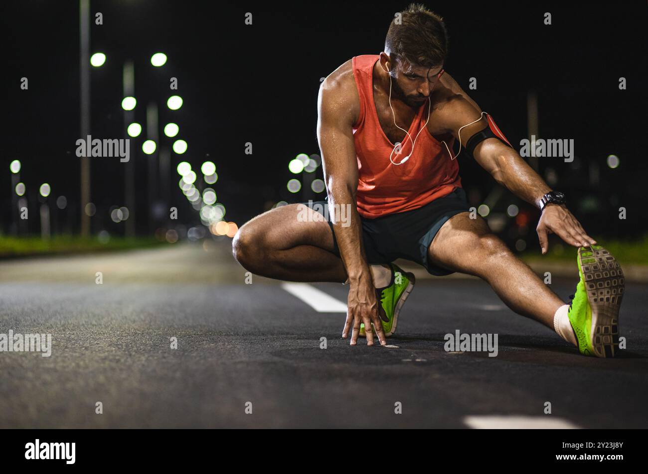 Man preparing to run through the city at night, he stretching his leg ...
