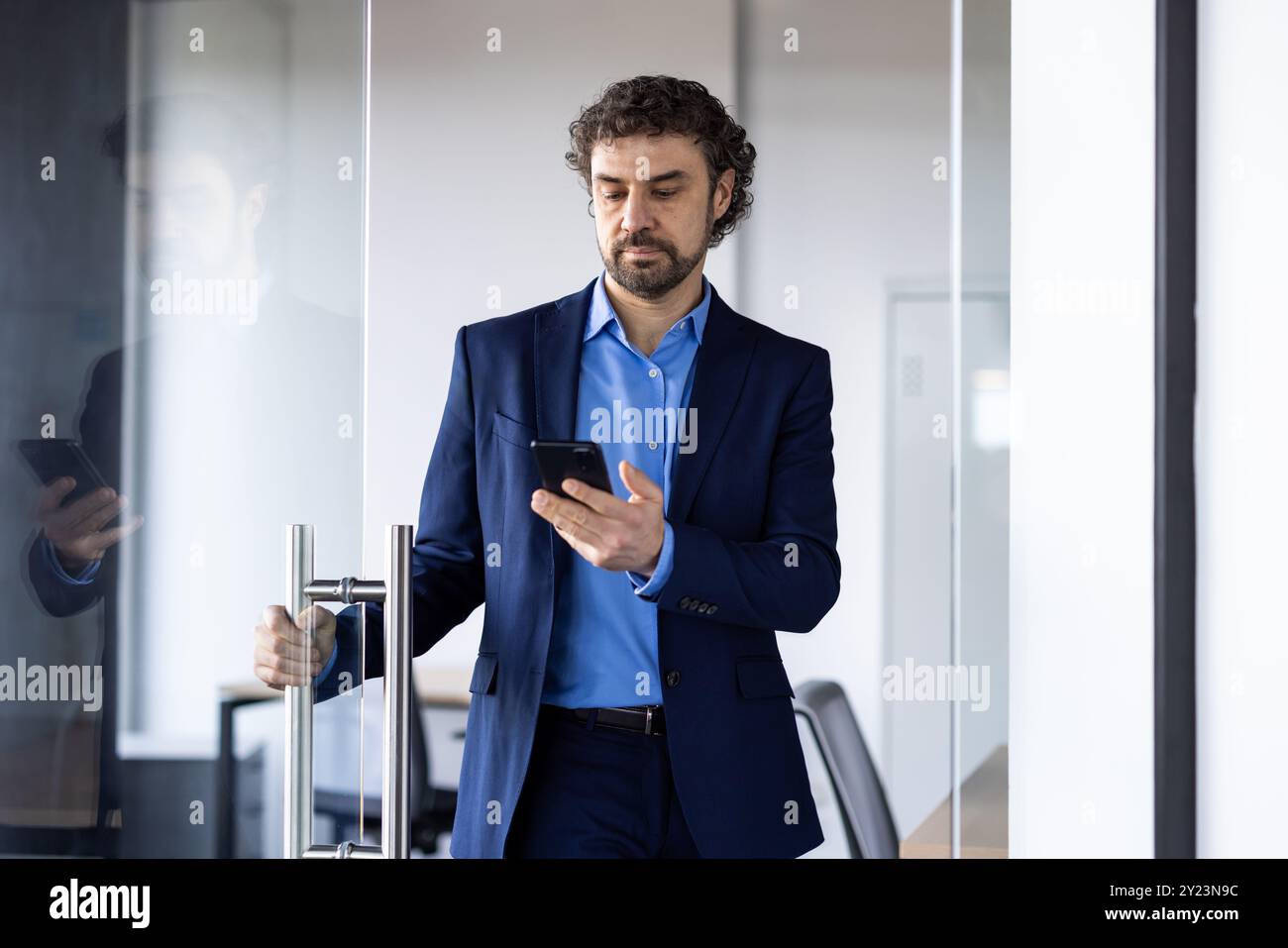 Serious businessman in blue suit uses smartphone while entering office ...