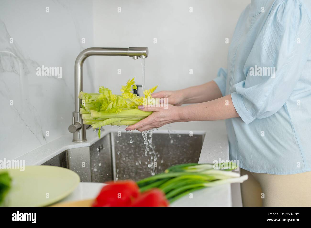 A woman is cleaning fresh vegetables in a modern kitchen to prepare a ...
