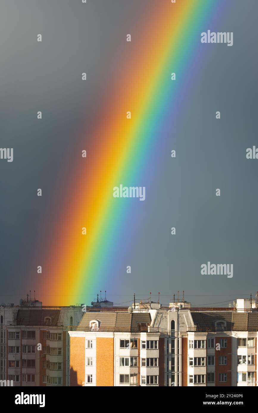 Bright colorful rainbow over city buildings in rainy day dark blue sky ...