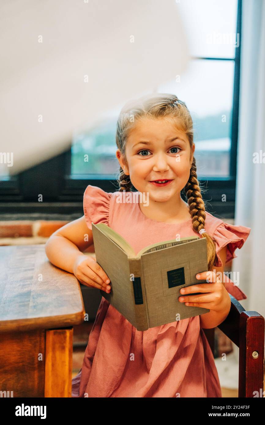 Young girl reading a book at a desk, smiling with excitement Stock ...
