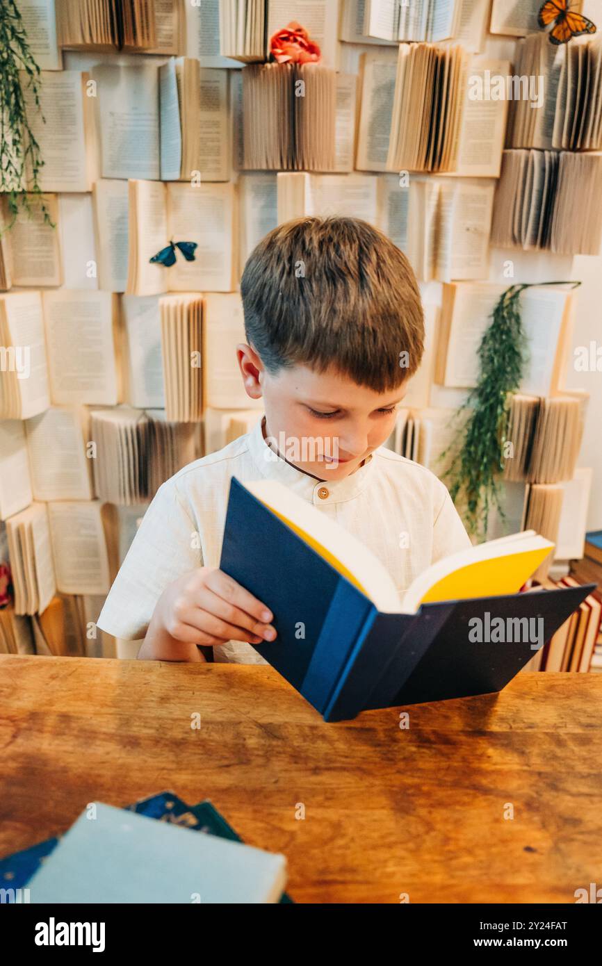 Boy reading a blue book at a wooden desk, with open books Stock Photo ...